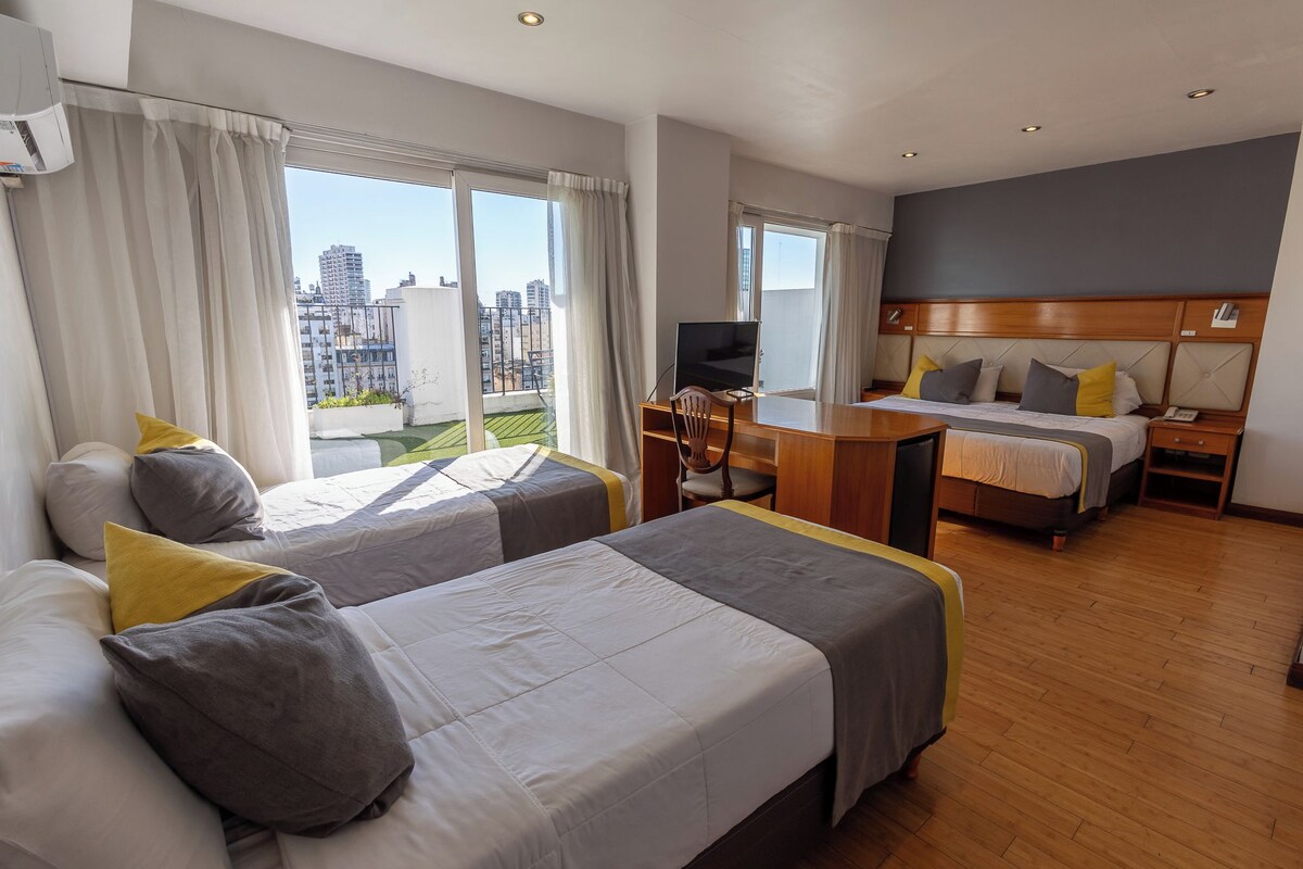 Quarto de hotel com duas camas, uma escrivaninha, uma cadeira e uma televisão.