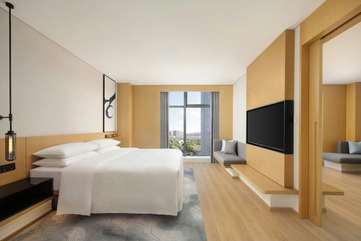 Quarto de hotel moderno com uma cama grande, TV de tela plana e vista para a cidade.