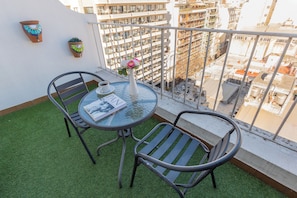 Uma varanda com mesa de vidro, duas cadeiras, um vaso de planta e uma revista.