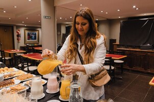 Uma pessoa servindo uma bebida em um jarro de vidro em uma mesa de buffet com diversos alimentos e bebidas.
