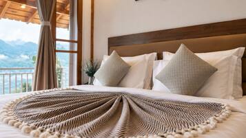 Cama com manta estampada, cabeceira de madeira e vista para montanhas pela janela.