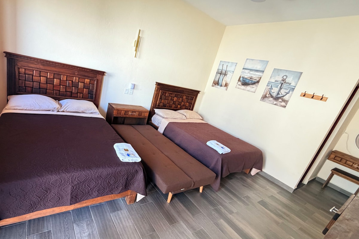 Quarto de hotel com duas camas, cabeceira de madeira, mesa de cabeceira e parede com arte decorada com tema náutico.