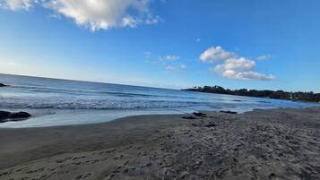 Uma praia com pegadas na areia, céu claro e uma linha de costa distante com árvores.