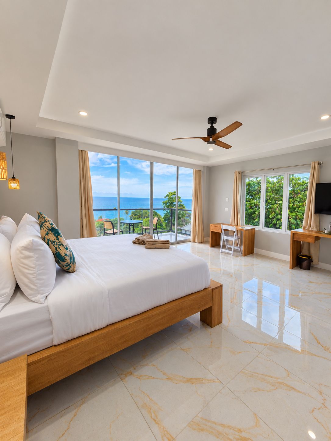 Quarto espaçoso com uma cama grande, ventilador de teto, escrivaninha e vista para o mar.