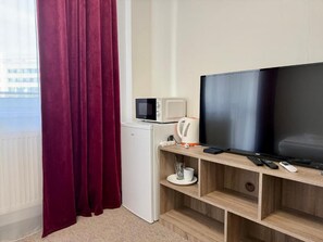 Quarto compacto com televisão, micro-ondas e pequeno frigorífico.