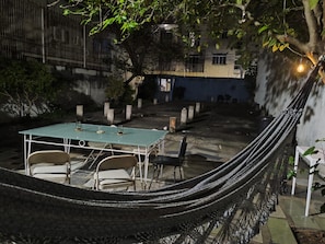 Uma área externa com mesa e cadeiras, uma rede e um vaso de planta.