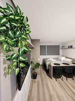 Quarto moderno com cama, mesa de cabeceira e uma grande planta em vaso.