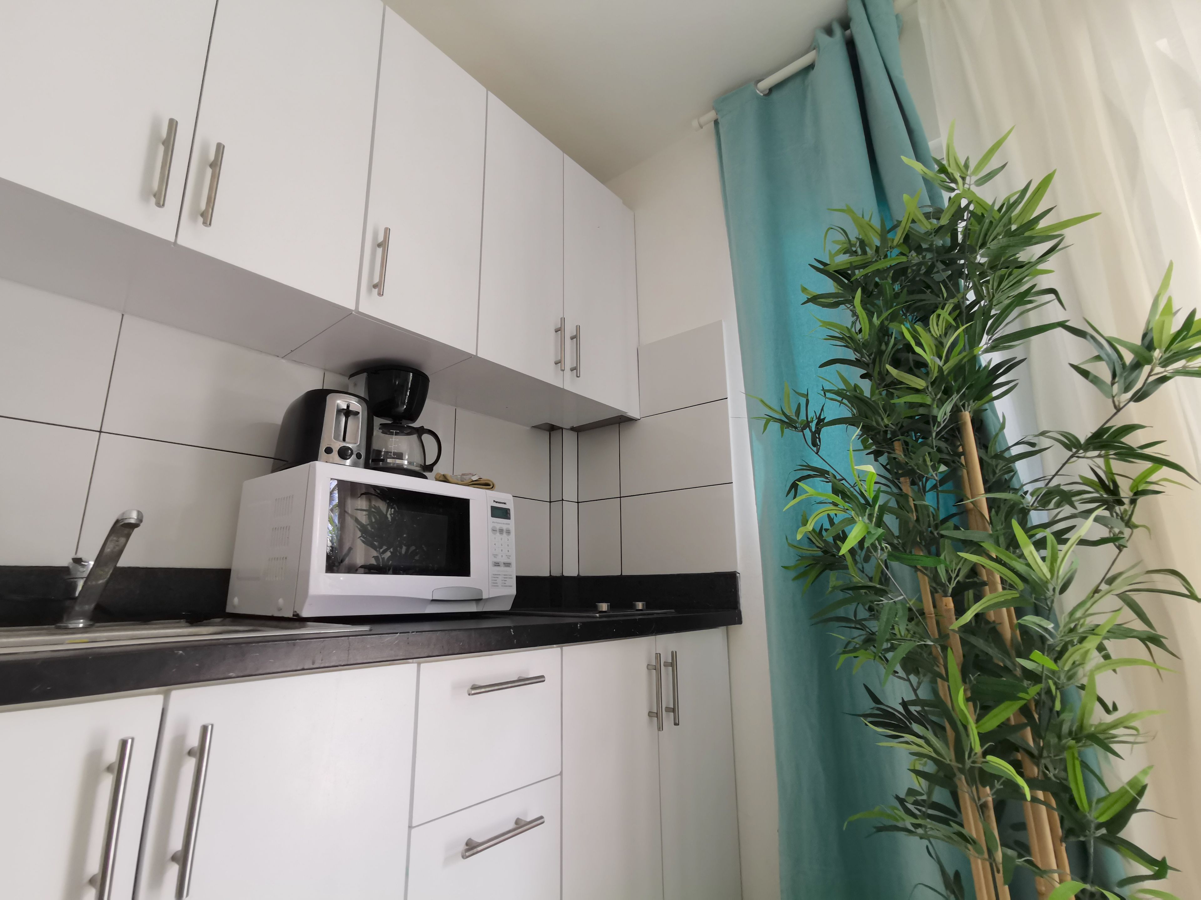 Cozinha com armários brancos, micro-ondas, torradeira e cafeteira no balcão.