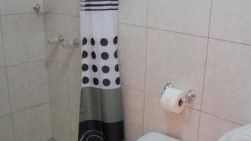 Casa de banho com sanita, cortina de chuveiro e suporte para rolo de papel higiénico.