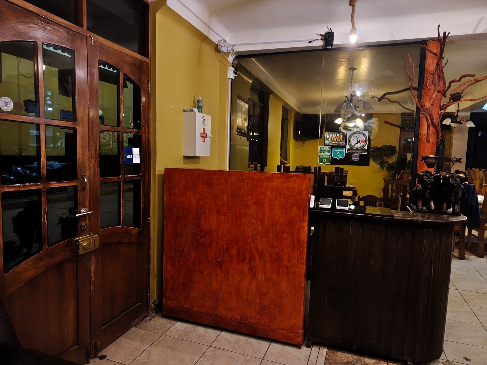 Uma área de bar com balcão de madeira, um registradora e uma placa fixada na parede.