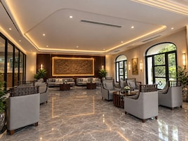 Um hall amplo com piso de mármore, área de estar com sofás e poltronas, um grande mural na parede e janelas grandes com painéis de vidro decorativos.