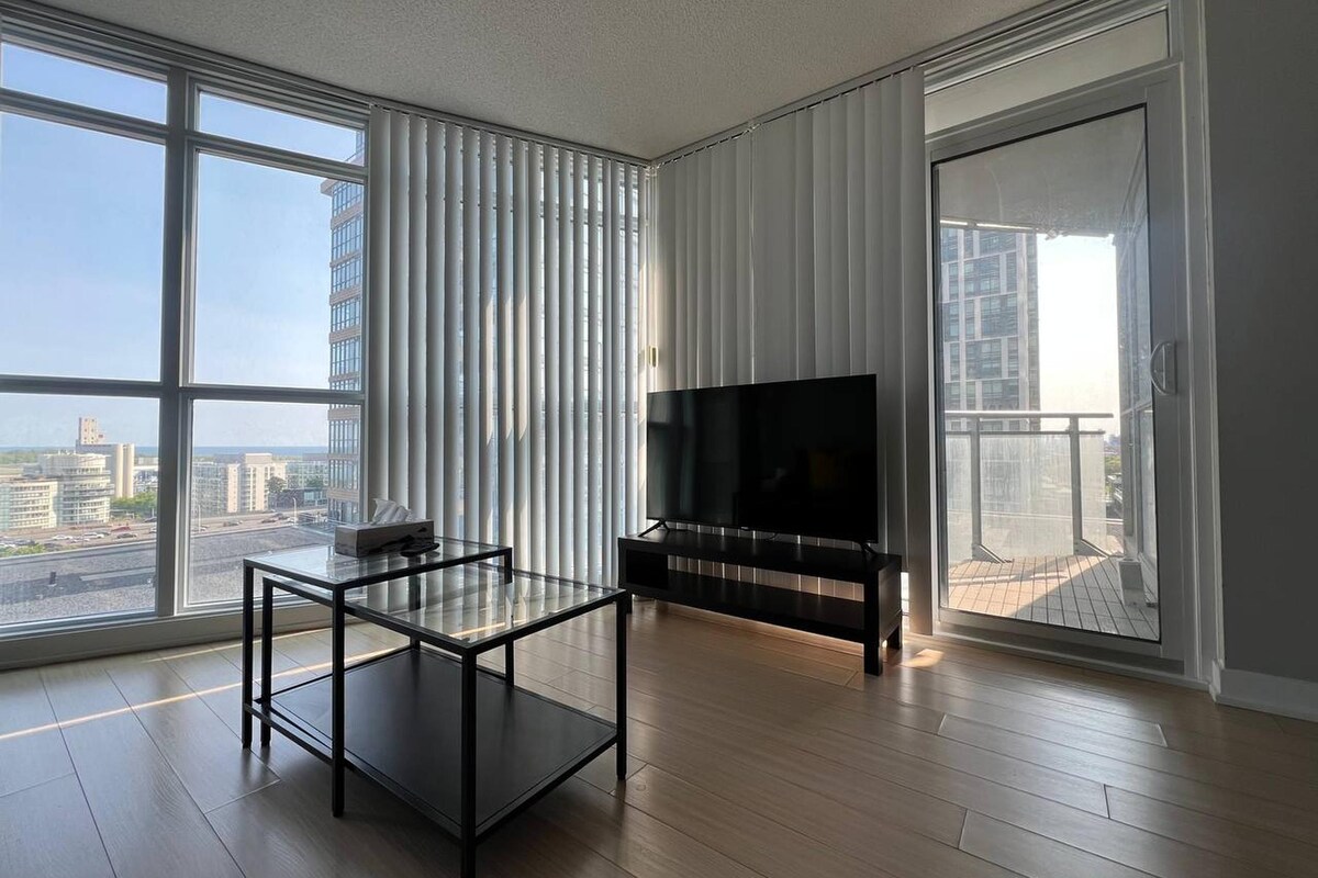 Uma sala de estar moderna com uma janela grande, uma televisão de tela plana e uma mesa de centro de vidro.