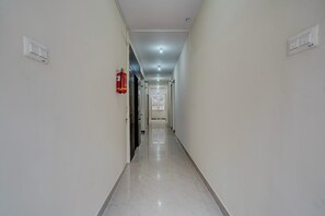Corredor com extintor fixado na parede, uma porta no final e uma luminária no teto.