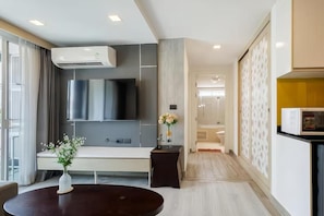 Quarto de hotel moderno com televisão de tela plana, mesa de jantar, vaso com flores e vista para o banheiro.