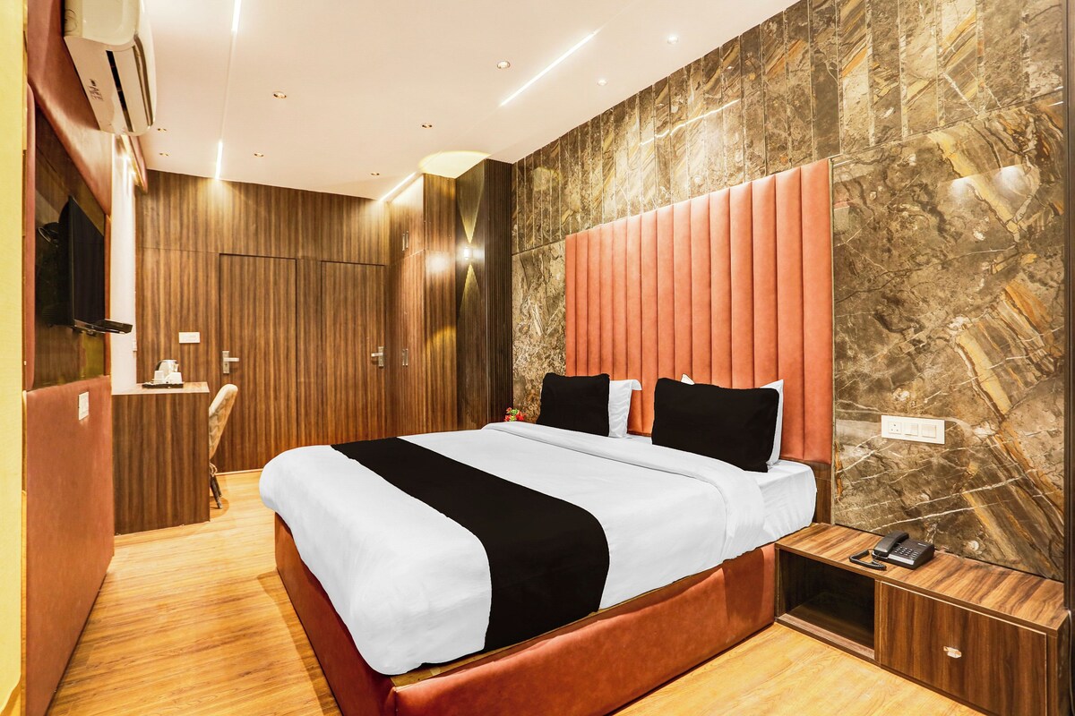 Quarto de hotel com uma cama grande, um guarda-roupa de madeira, uma escrivaninha com cadeira e uma parede com padrão de mármore.