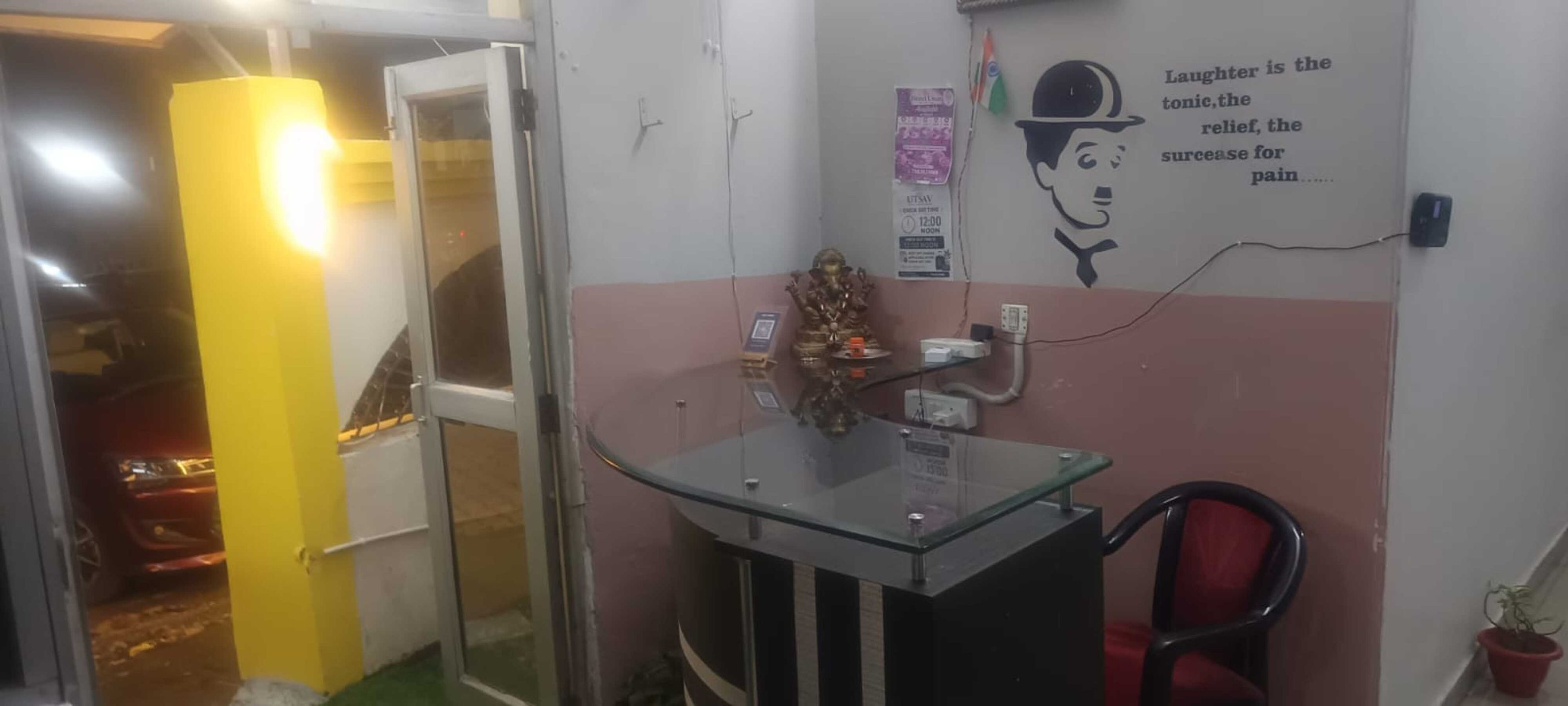 Quarto com divisória de vidro, uma cadeira, uma mesa pequena com uma estátua e parede com pôster e bandeira.