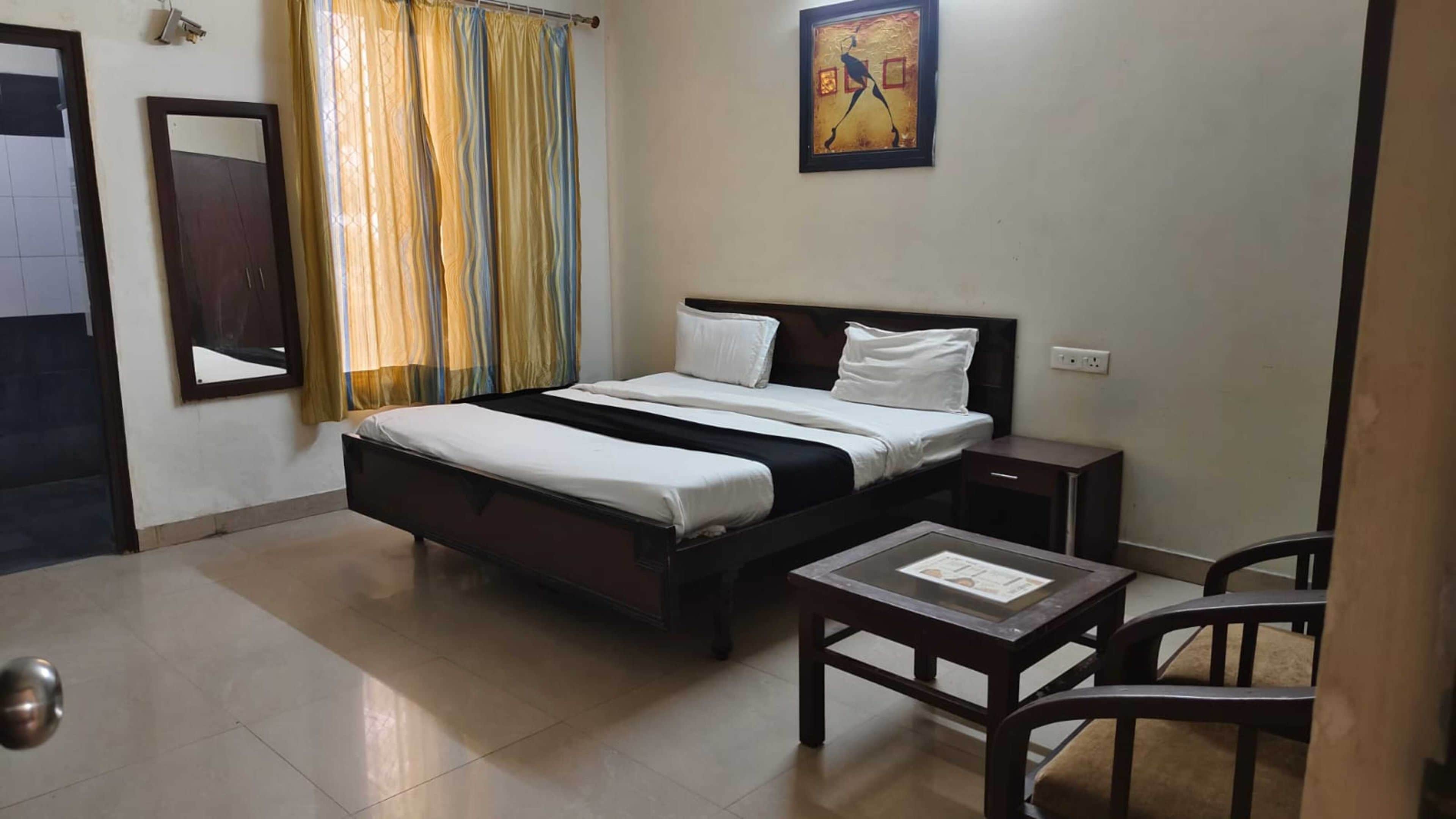 Quarto de hotel com cama, mesas de cabeceira, uma pequena mesa e uma cadeira.