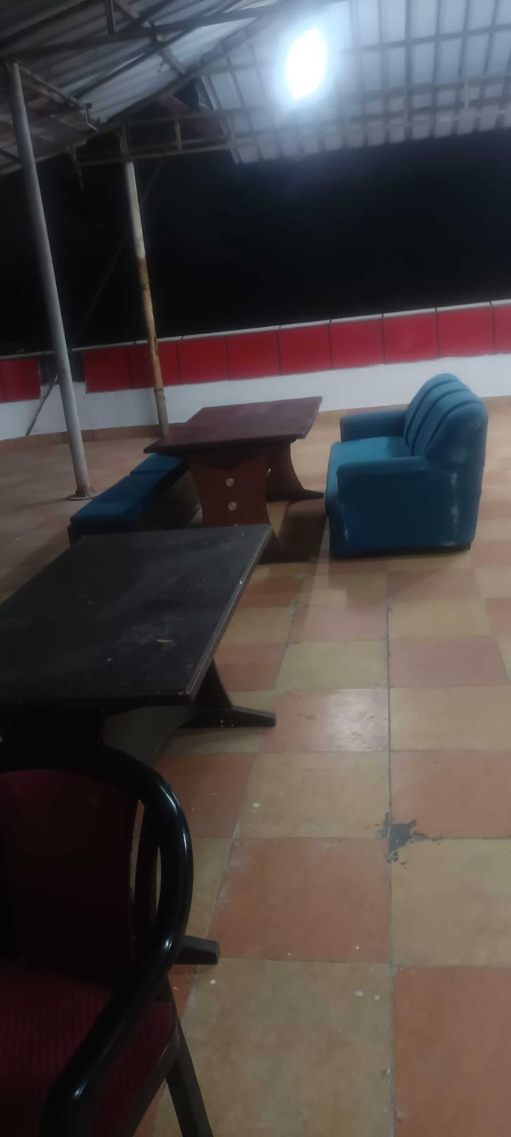 Área de estar coberta ao ar livre, com mesa e cadeiras, parede vermelha e branca, e piso de azulejos.