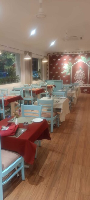 Restaurante com várias mesas, cada uma coberta por um tecido, e cadeiras com almofadas.