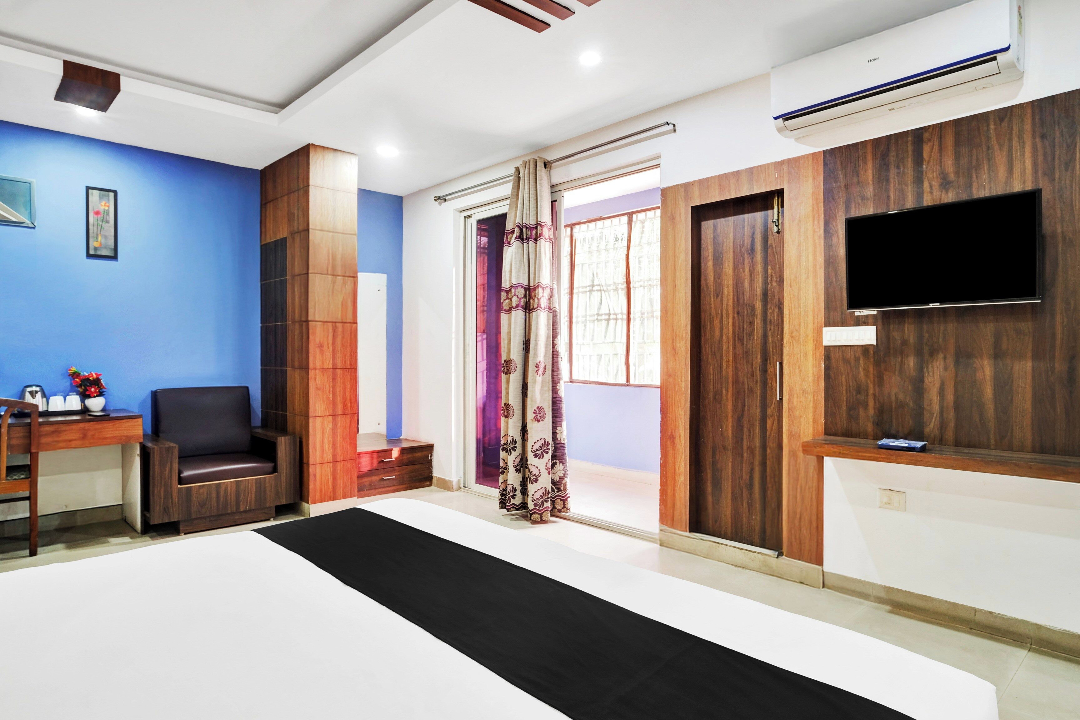 Quarto de hotel com uma cama, uma escrivaninha com cadeira, televisão e janela com cortinas.