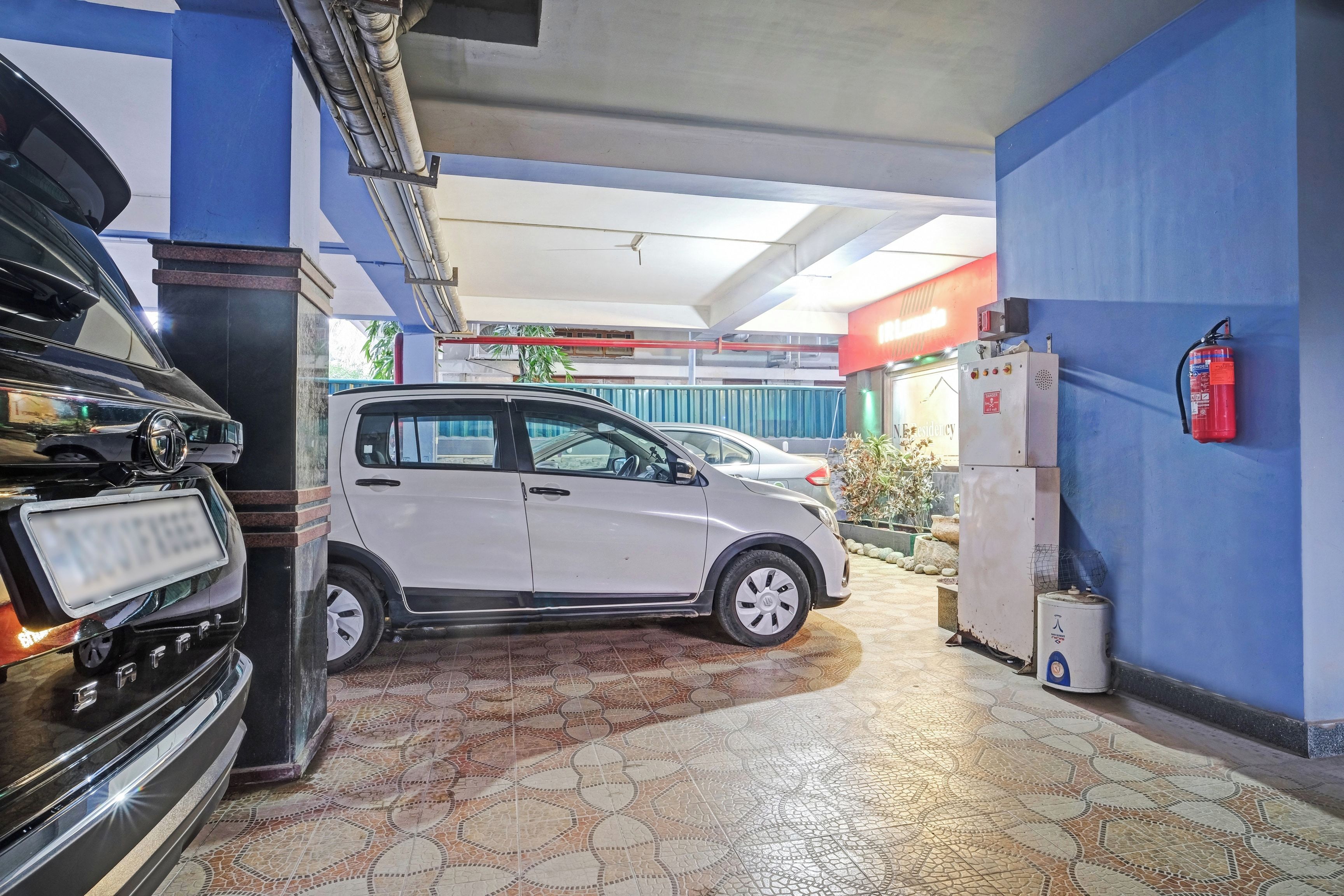 Uma garagem de estacionamento com um carro branco estacionado no interior, um extintor de incêndio fixado na parede e um bebedouro no chão.
