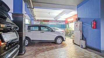 Uma garagem de estacionamento com um carro branco estacionado no interior, um extintor de incêndio fixado na parede e um bebedouro no chão.