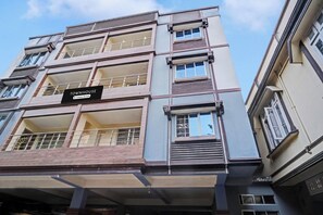 Um edifício de vários andares com varandas, uma placa indicando que é propriedade corporativa com serviços, e céu azul ao fundo.