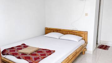 Uma cama de solteiro com cabeceira de madeira, roupa de cama branca e um cobertor vermelho estampado.