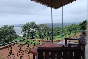 Uma varanda com vista para o mar e colinas, uma mesa e uma cadeira.