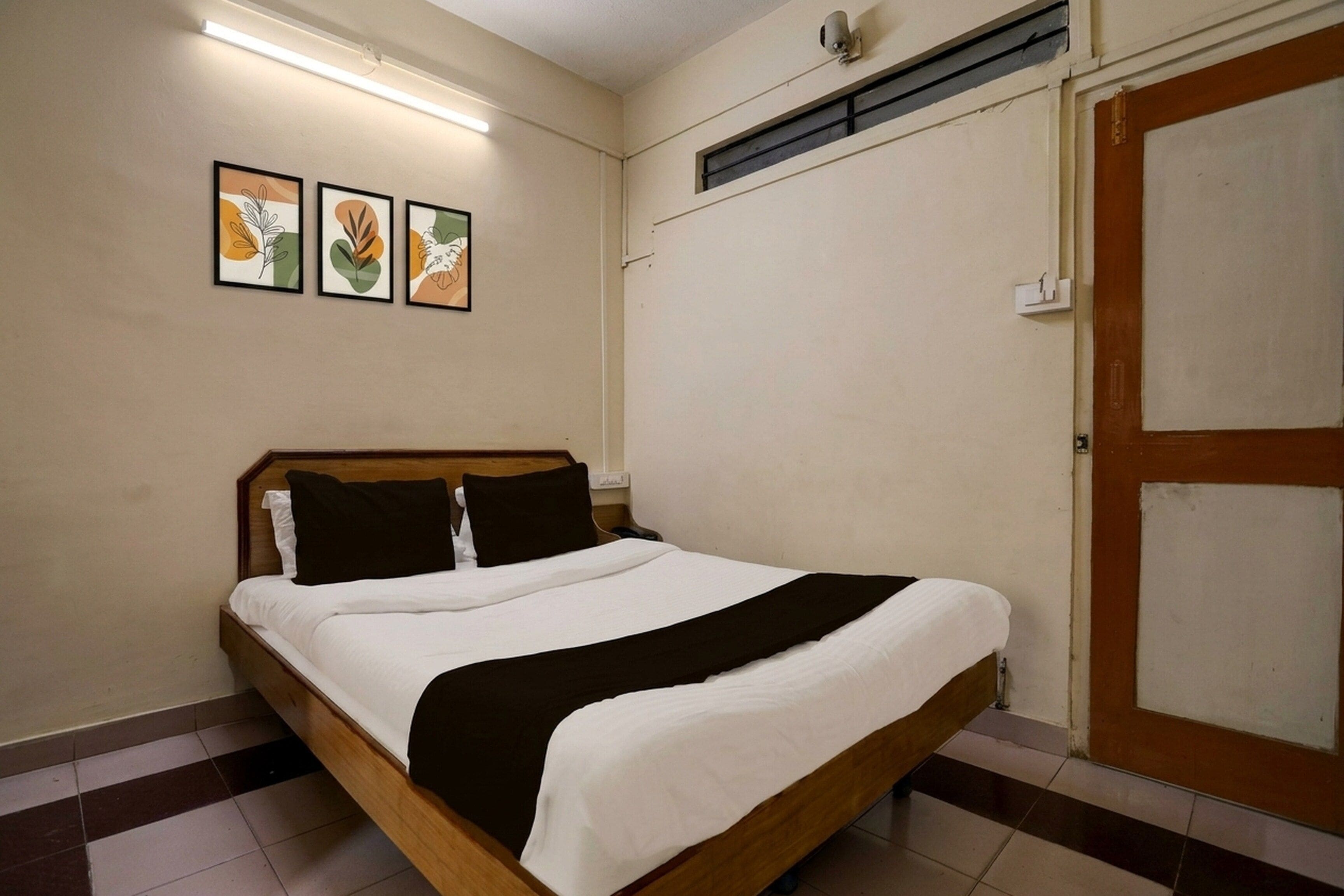 Quarto de hotel com cama, porta e três quadros na parede.