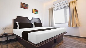 Quarto de hotel com cama grande, mesa de cabeceira com telefone, ar condicionado e janela com cortinas.