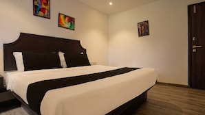 Quarto de hotel com uma cama grande, cabeceira de madeira e três quadros na parede.