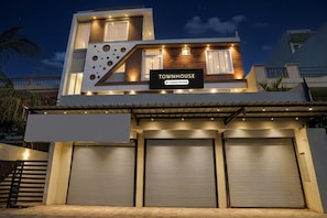 Uma casa geminada moderna com uma placa indicando que oferece serviços corporativos. Possui três portões de garagem e uma fachada única com recortes circulares.