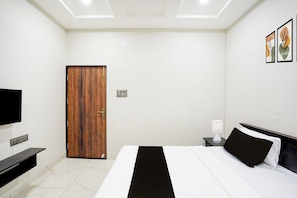 Quarto de hotel com cama, mesa de cabeceira, abajur e televisão fixada na parede.