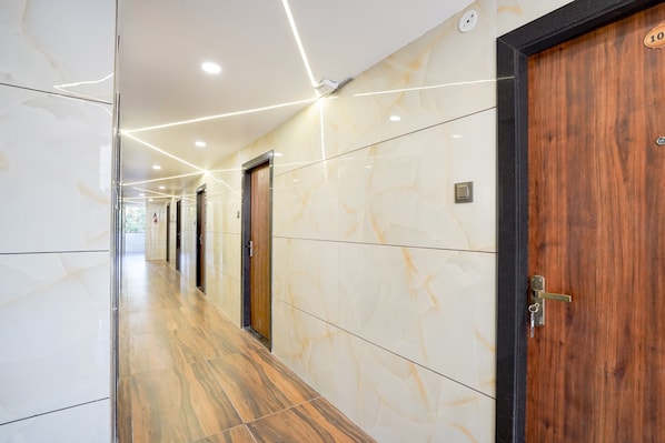 Um corredor com paredes de mármore, portas de madeira e chão de azulejos.