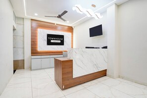 Uma área de recepção com balcão de mármore, ventoinha no teto e televisão montada na parede.
