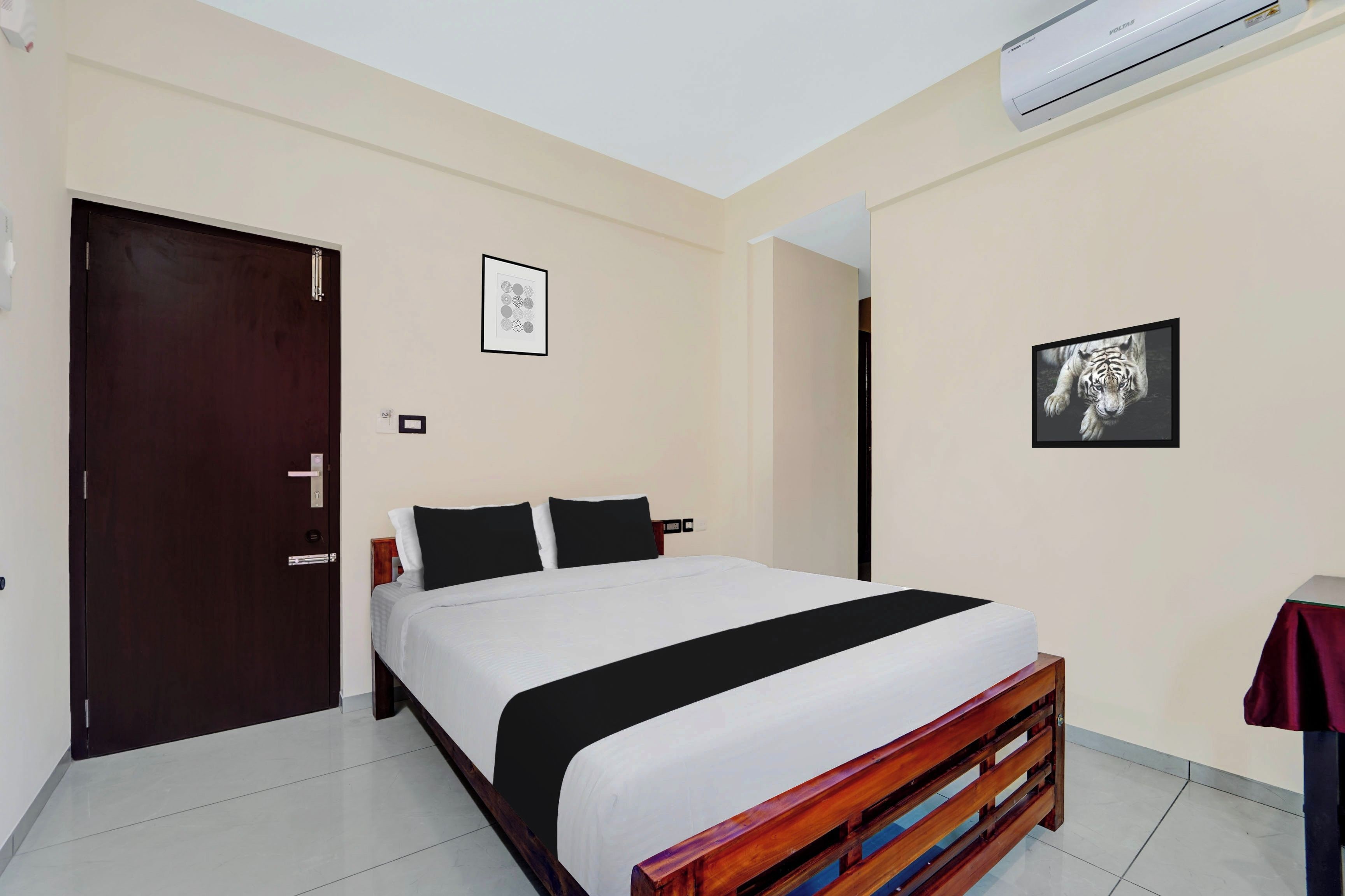Quarto de hotel com cama, porta, aparelho de ar condicionado e duas quadros na parede.