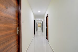 Corredor com portas de madeira de um lado e paredes brancas do outro, que leva a um quarto com janela.