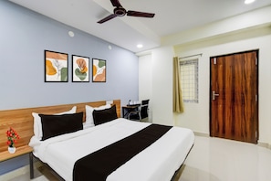 Quarto de hotel com cama, escrivaninha, cadeira, ventilador de teto e obras de arte na parede.