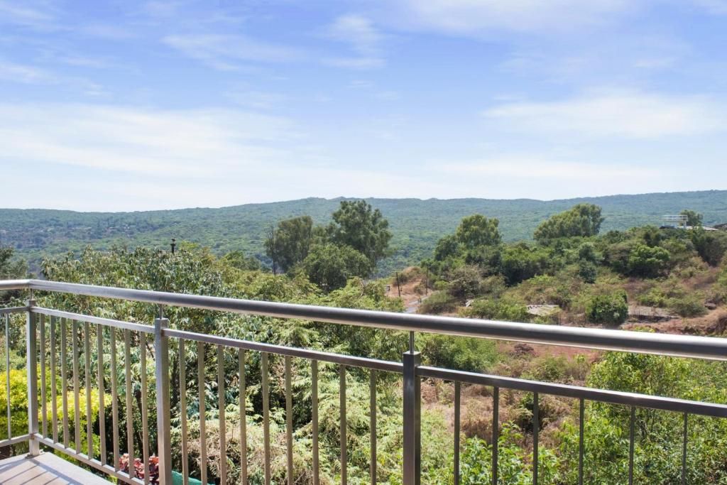 Varanda com guarda-corpo metálico com vista para uma paisagem verdejante, com árvores e colinas.