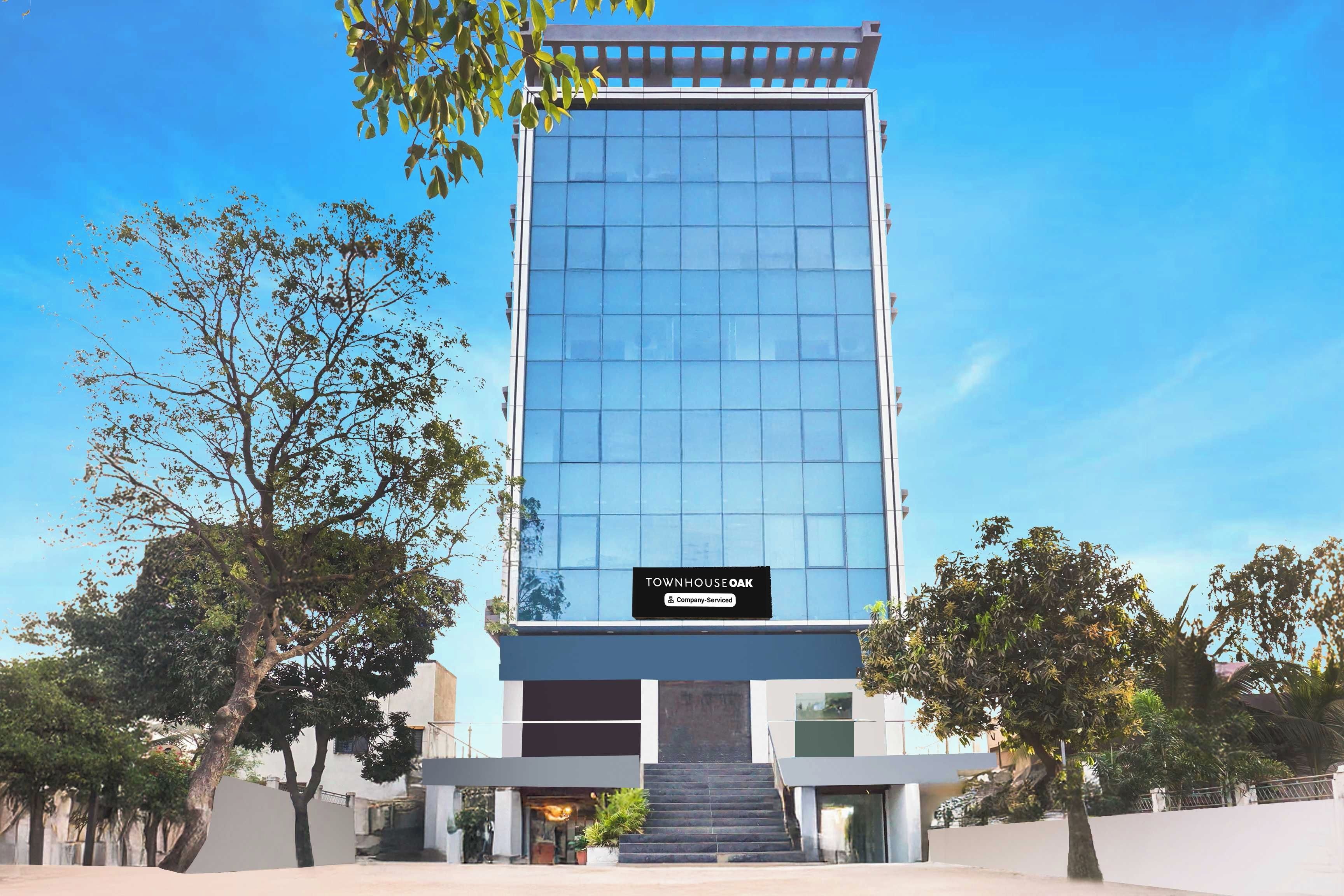Um edifício moderno com fachada de vidro, uma placa com a inscrição 'TOWNHOUSE OAK Company Serviced' e uma escadaria que leva à entrada.