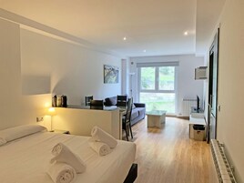 Quarto de hotel com cama, escrivaninha, cadeira, sofá e janela.