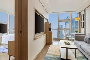 Quarto de hotel com cama, escrivaninha, sofá, televisão e uma grande janela com vista para a cidade.