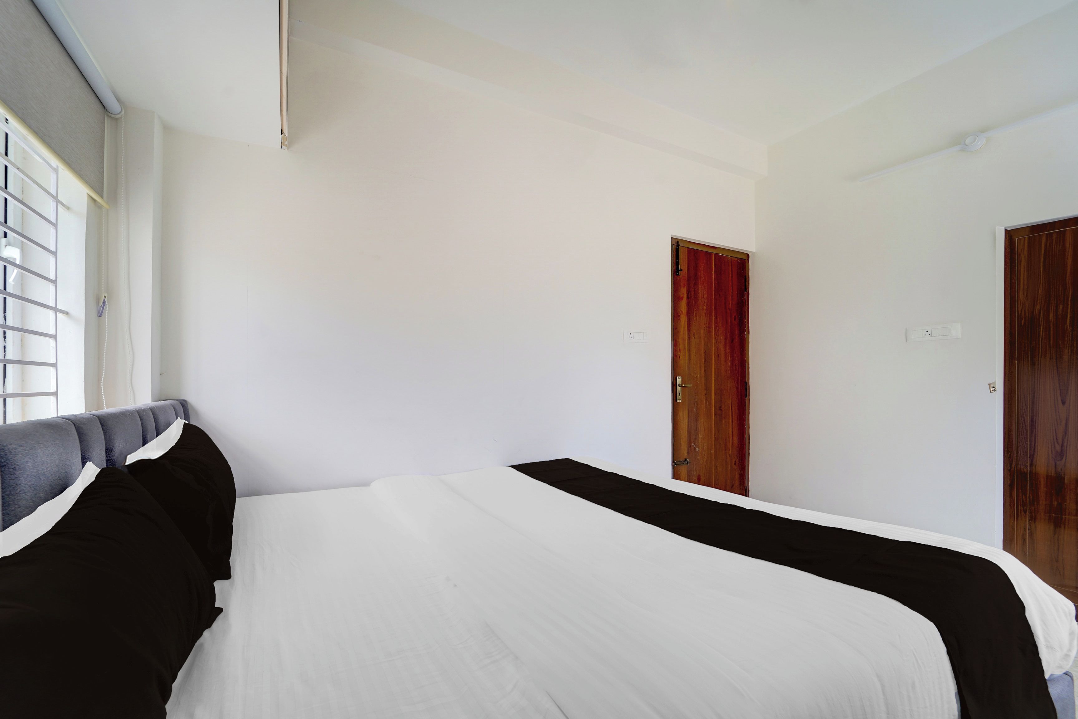 Quarto com cama, janela com persianas, porta e interruptor de luz na parede.