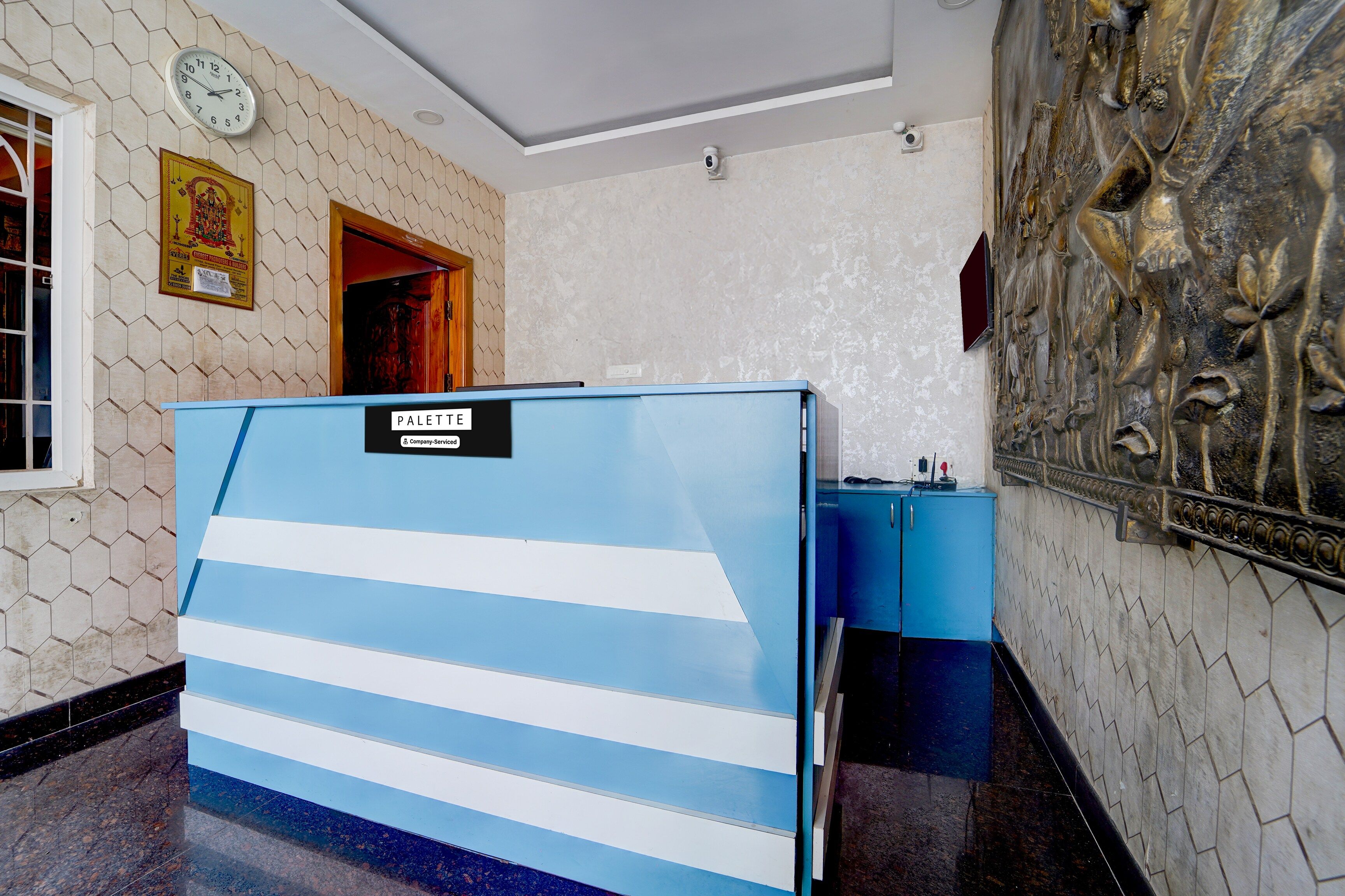Quarto de hotel com divisória azul, relógio na parede e um objeto decorativo na parede.