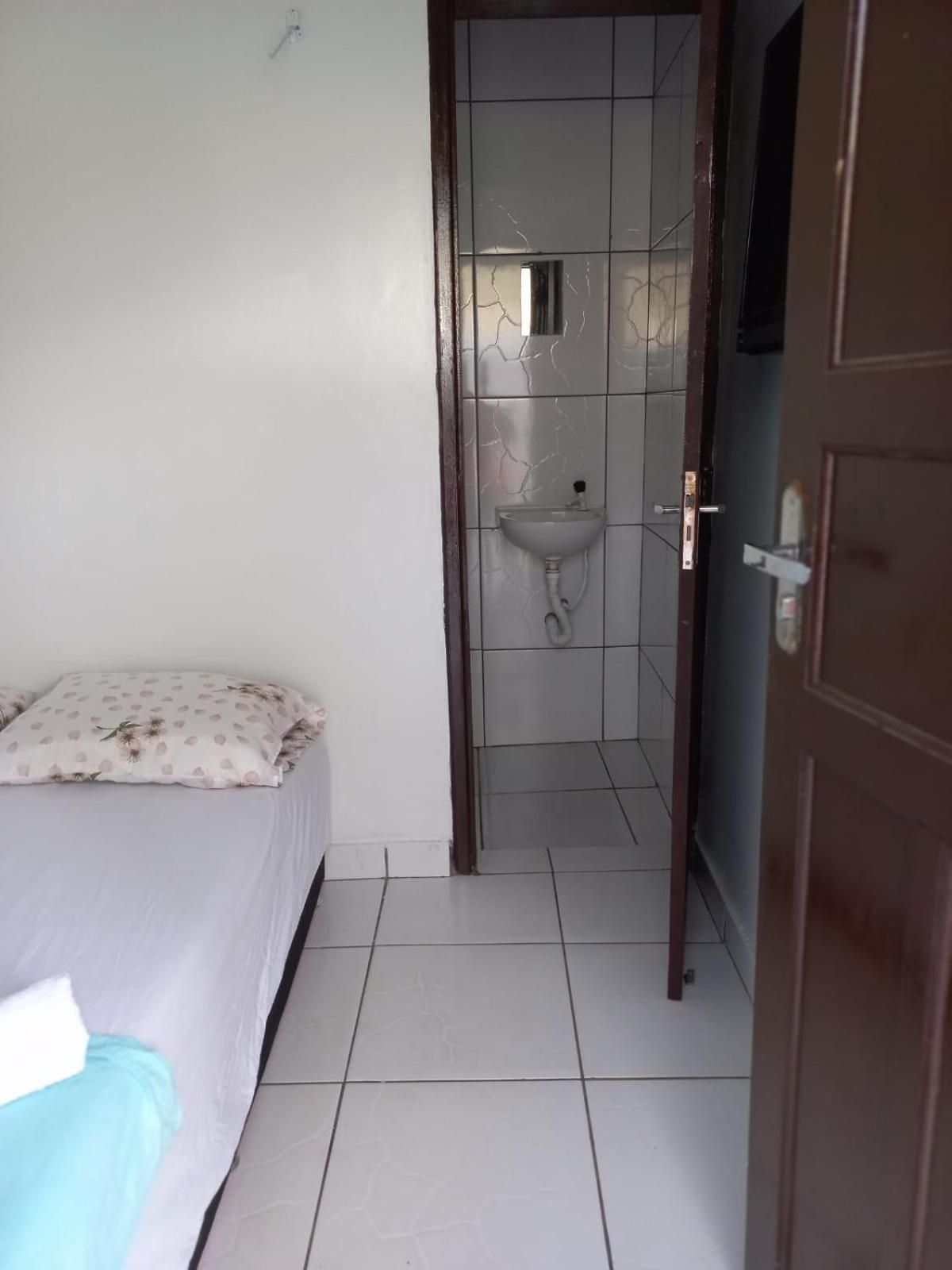 Quarto com cama, mesa de cabeceira e porta para um banheiro com pia.