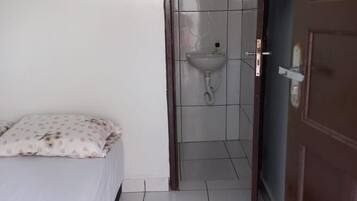 Quarto com cama, mesa de cabeceira e porta para um banheiro com pia.