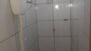 Casa de banho com azulejos brancos, sanita, chuveiro e suporte de papel higiénico fixado na parede.