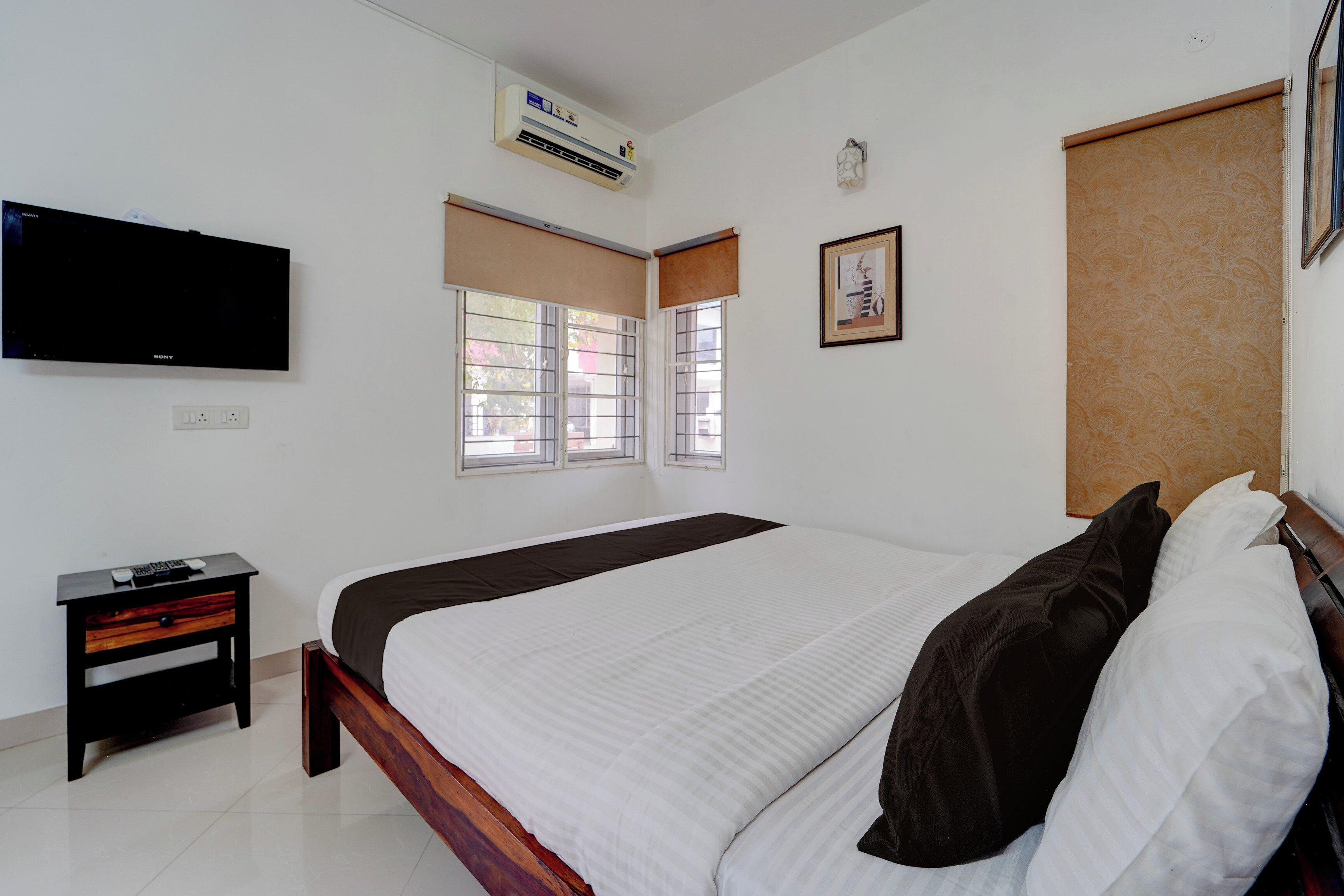 Um quarto com uma cama, uma TV, uma mesa de cabeceira e uma janela.