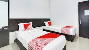 Quarto de hotel com duas camas, cabeceira escura, paredes brancas e uma porta com uma placa.